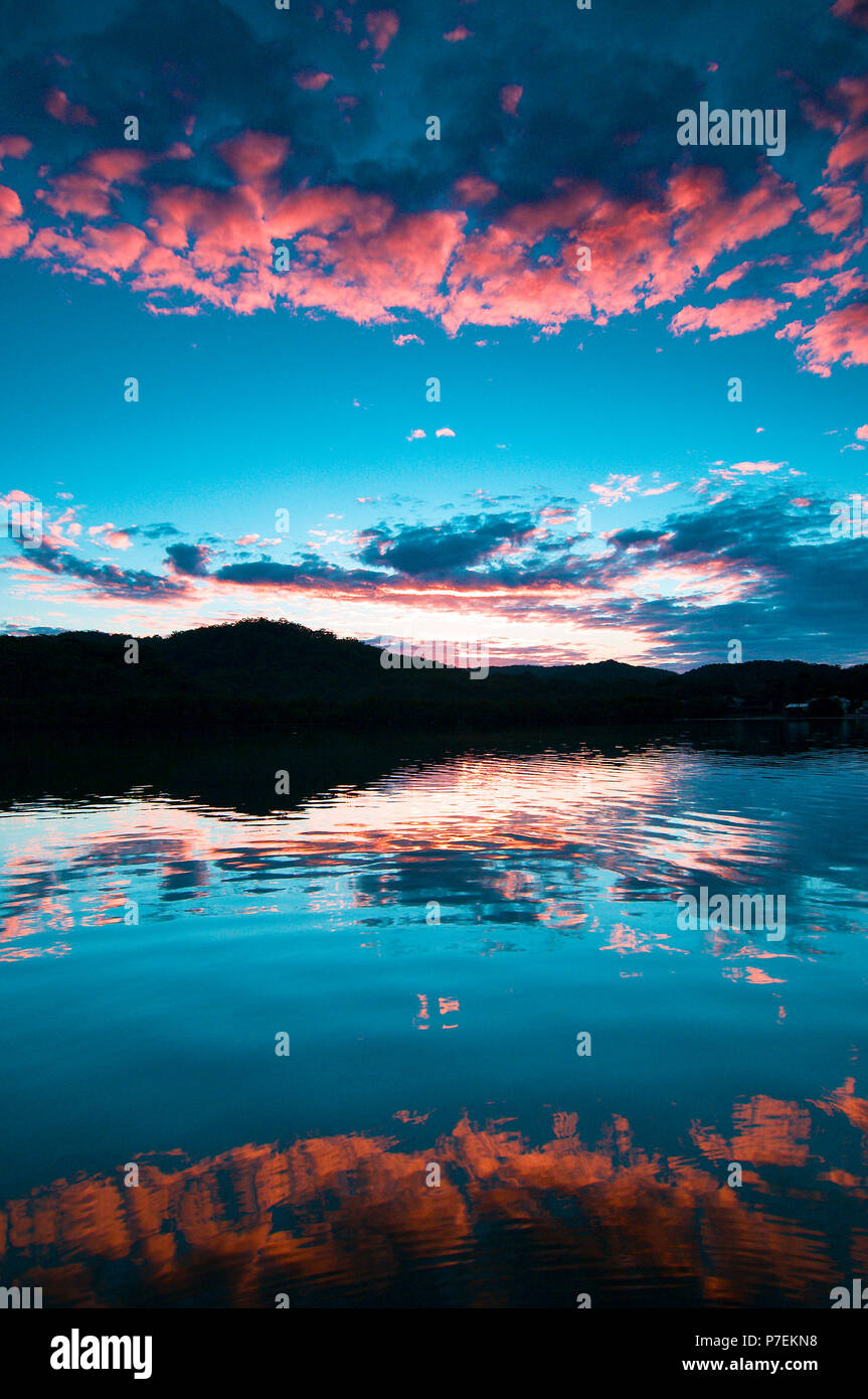 A colourful pink colored cloudy sunrise seascape over sea water with ...