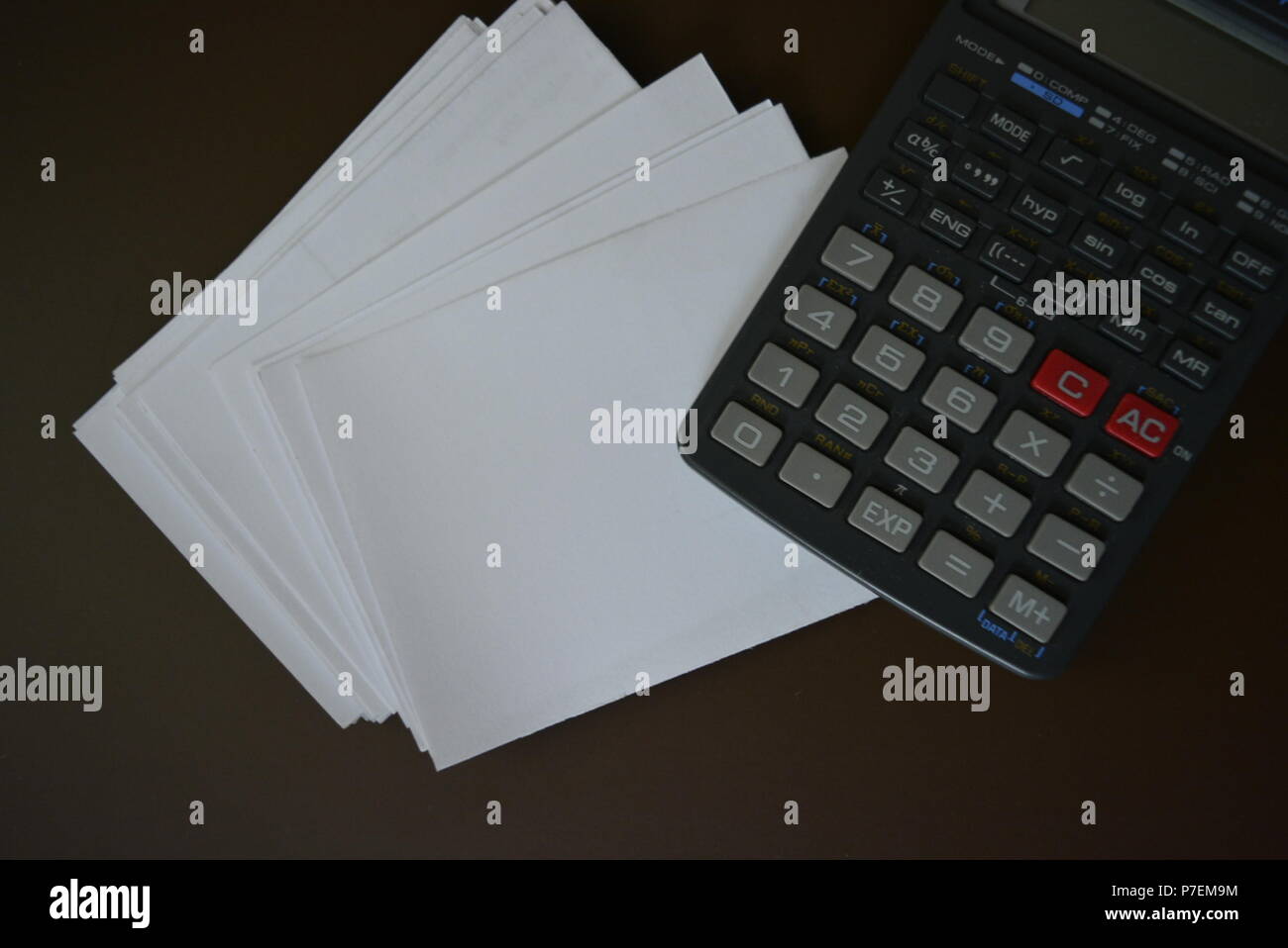 White sheets of paper and gray calculator on a brown matte background ...