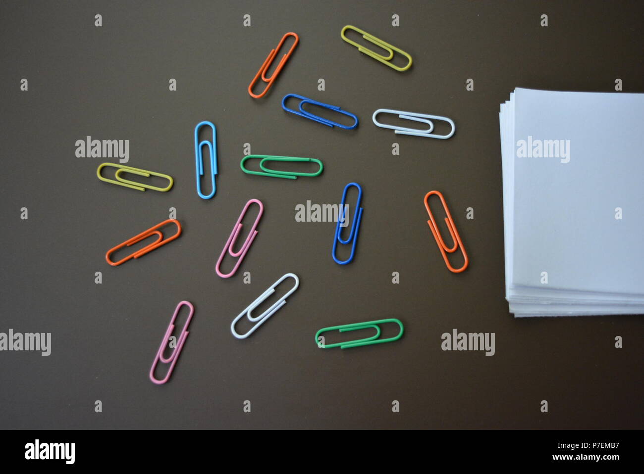 Colored paper clips laid out with a question mark and with sheets of ...