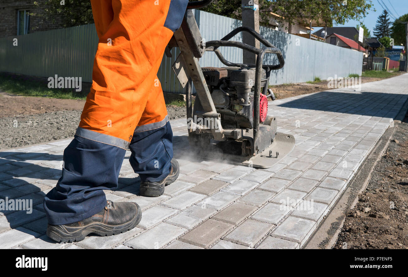 Man in orange uniform using vibrational paving stone machine for finish ...