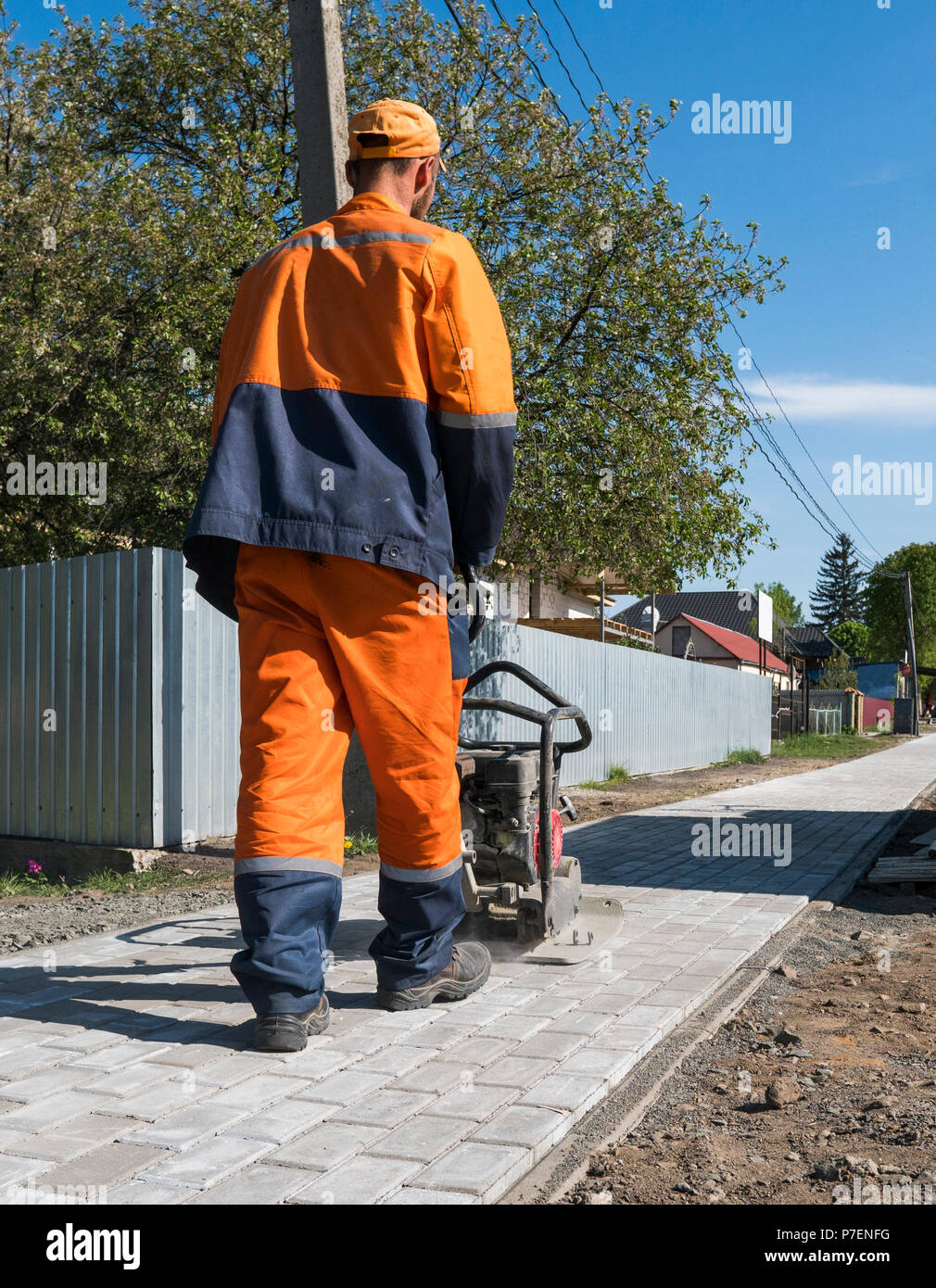 Man in orange uniform using vibrational paving stone machine for finish ...