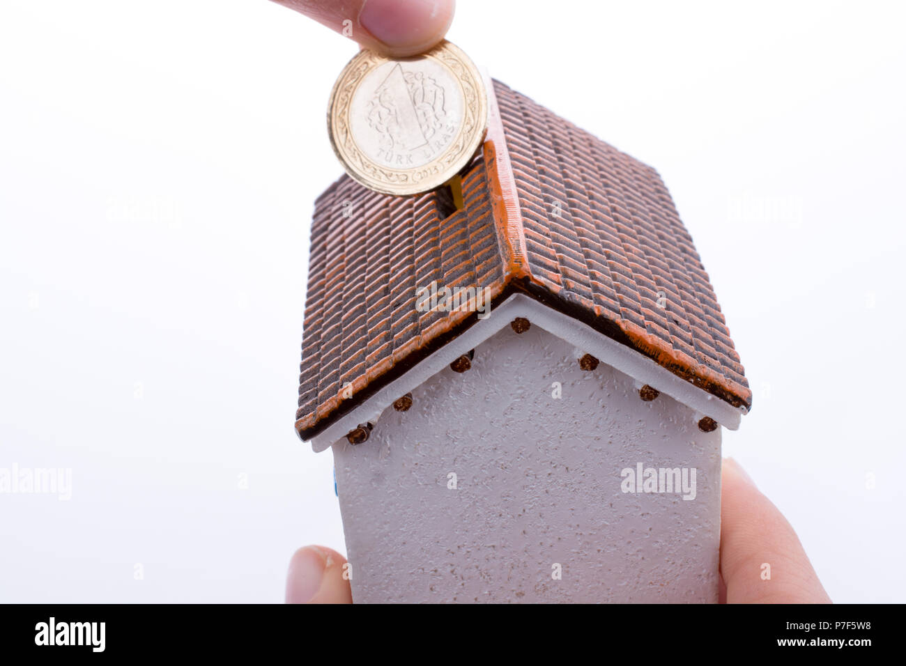 Hand dropping coin into the moneybox in the shape of a model house ...
