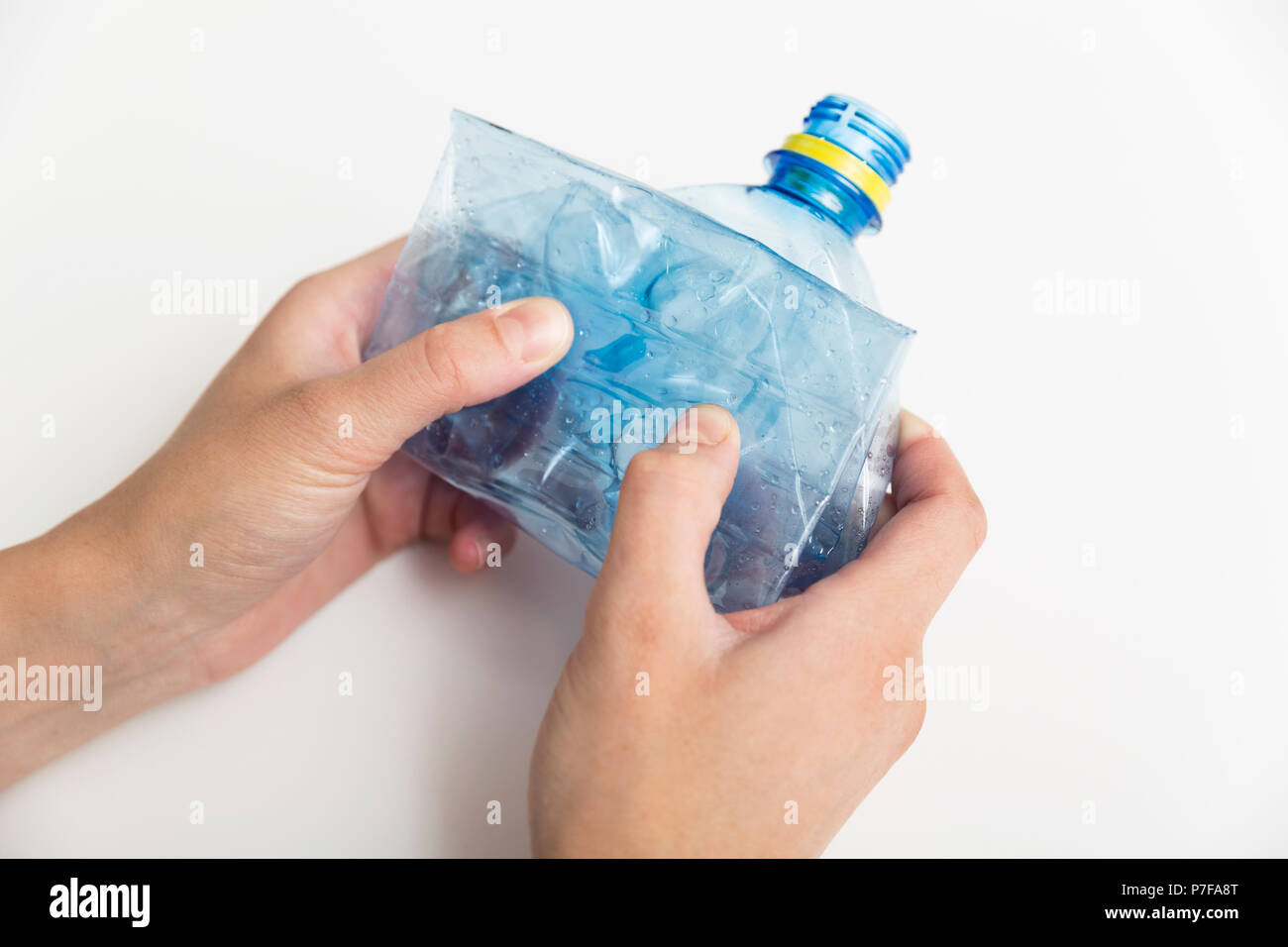 Crushed blue plastic bottle in woman's hands on white background ...