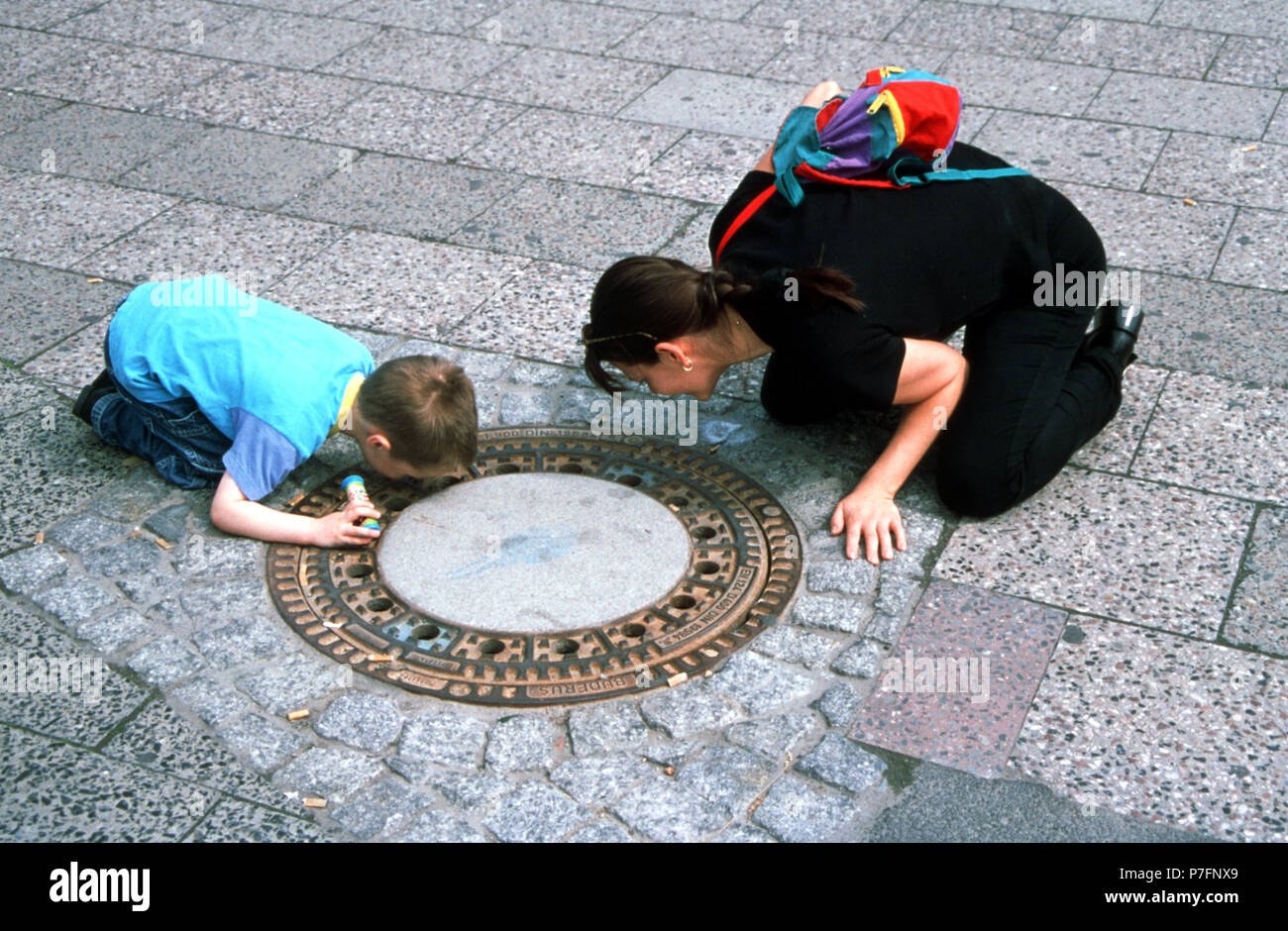 Mother and child looking in manhole cover, Berlin, Germany Stock Photo ...