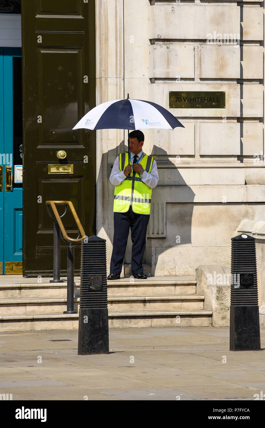 A security guard in Whitehall uses an umbrella as a sun shade during ...