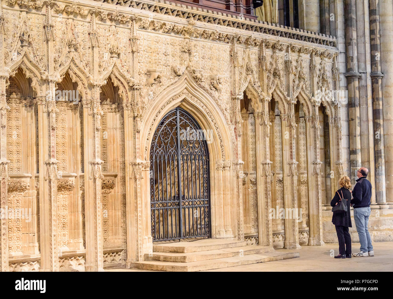 A man and a woman look closely at the carvings on the stone rood screen ...