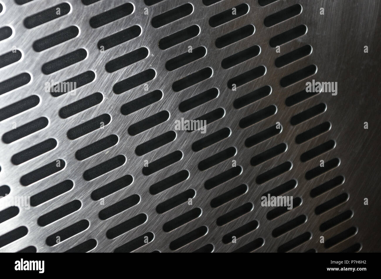 stainless steel grating with oblong holes on black background, close-up ...