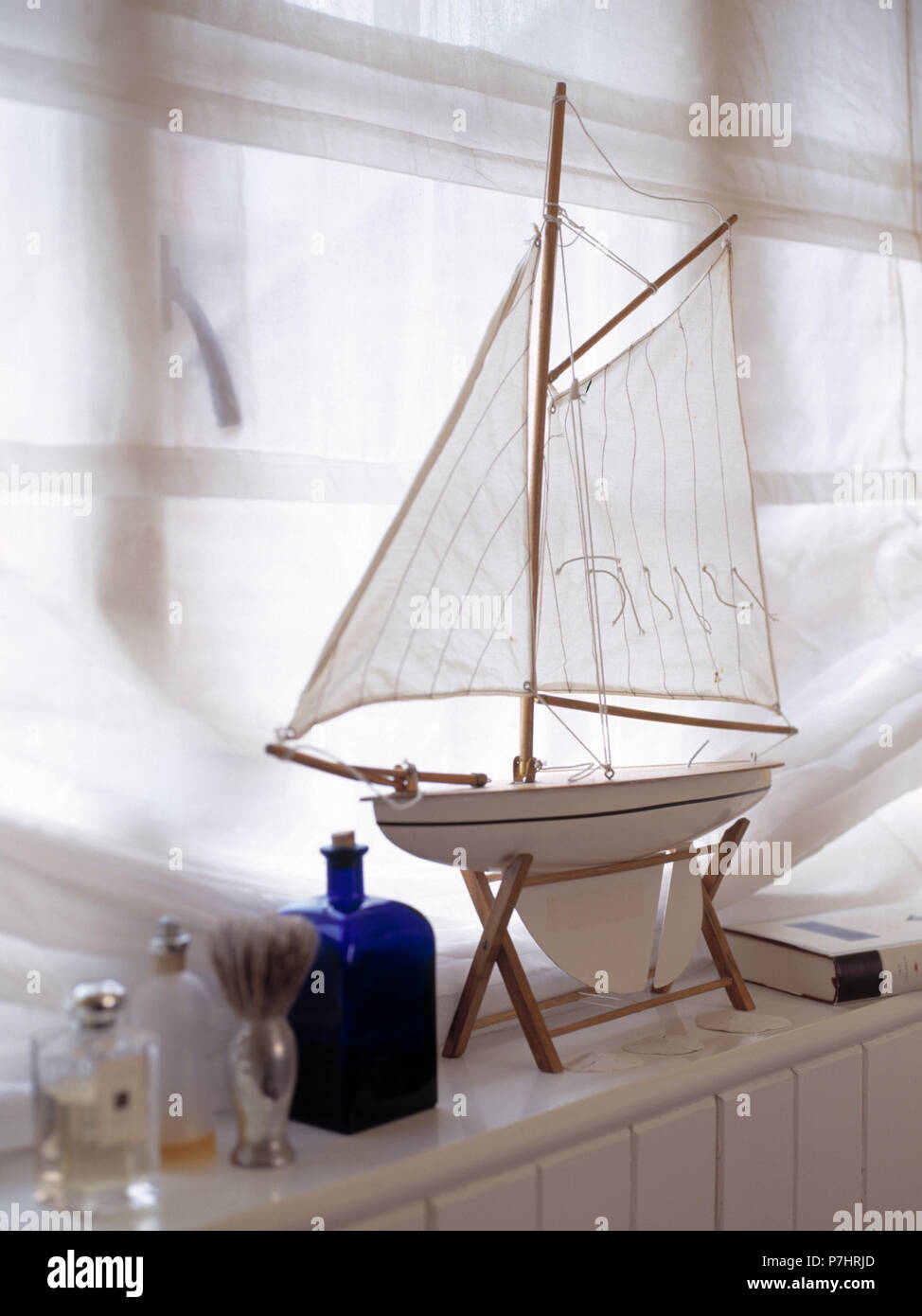 White model boat on window ledge against sheer white window covering ...