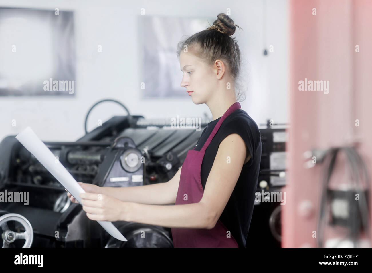 Woman standing by a printing press holding a piece of paper Stock Photo ...
