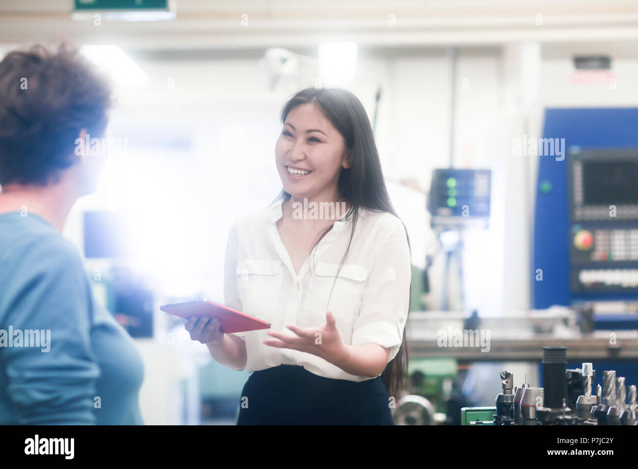 Smiling female engineer standing in a workshop talking to a colleague ...