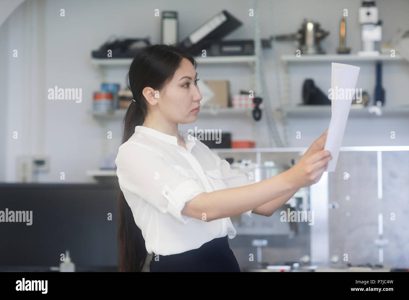 Female engineer standing in a workshop looking at technical drawings ...