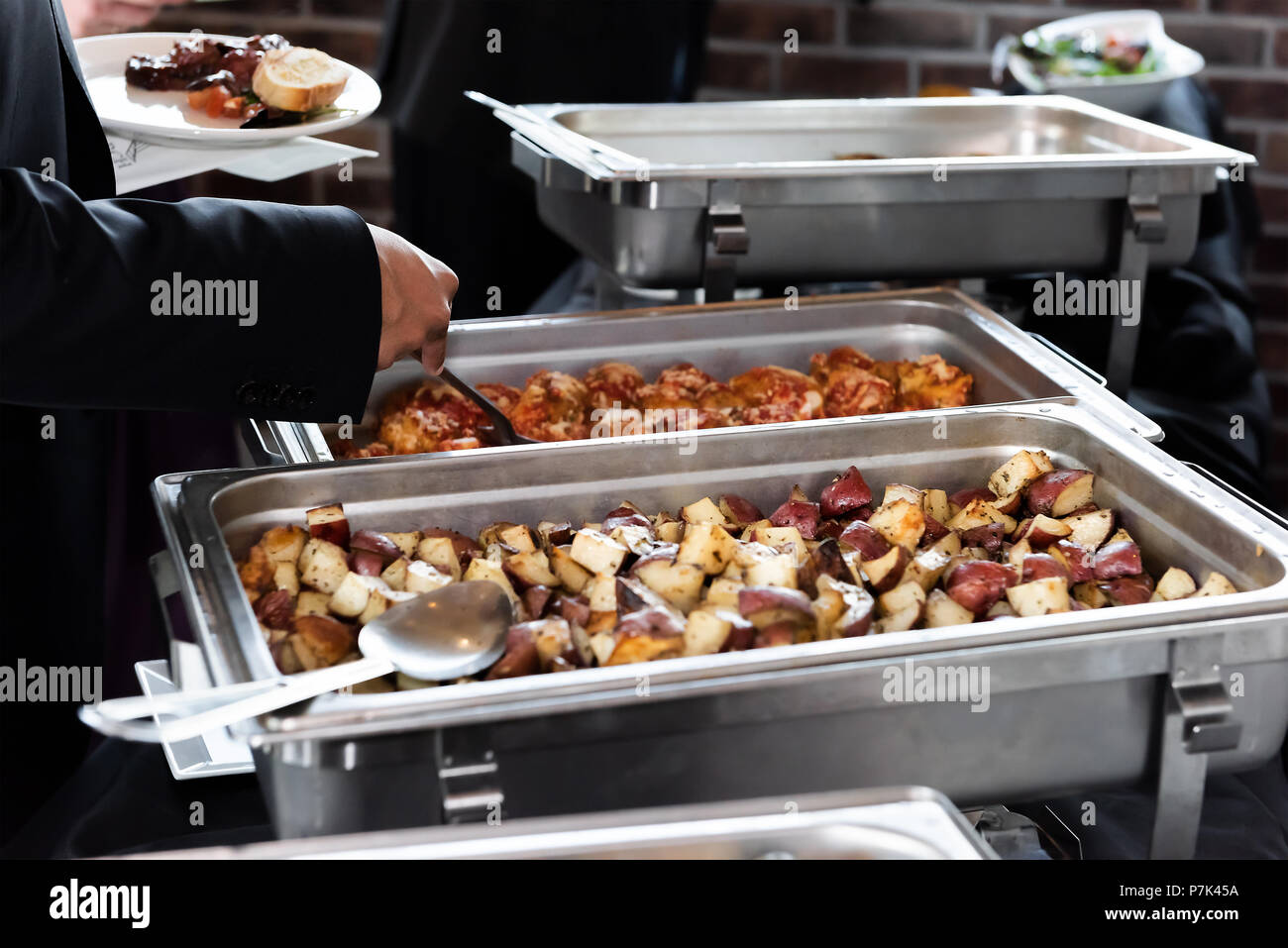 Hot buffet tray, fresh roasted potatoes, chicken with closeup of man ...