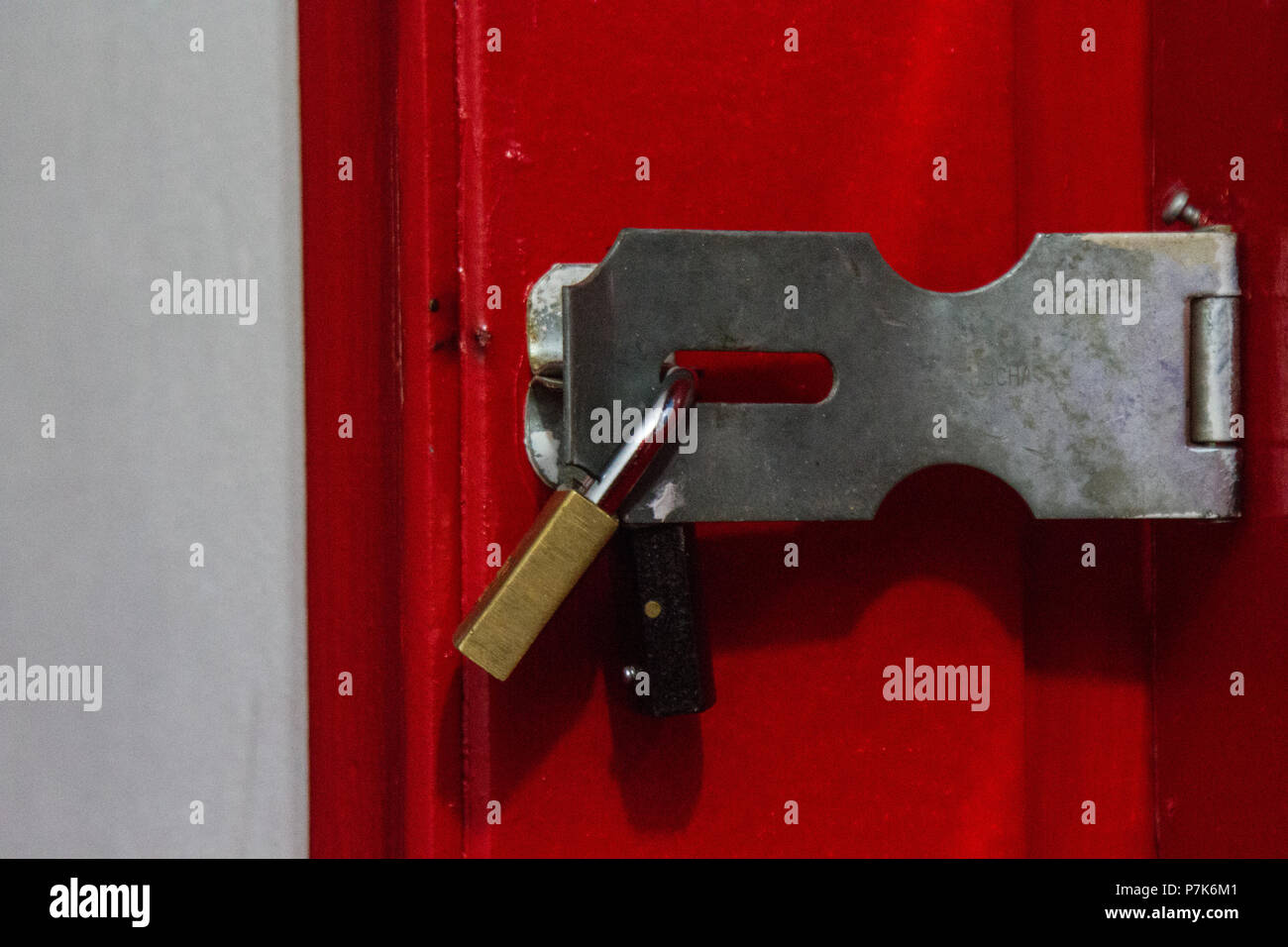 A padlock locks a home shiny red wood door in a white wall in a ...