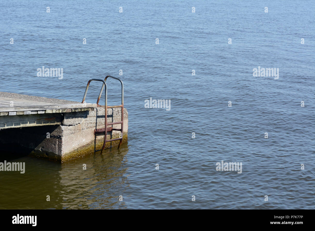 Rusted metal ladder on the side of a jetty, reaching down into water ...