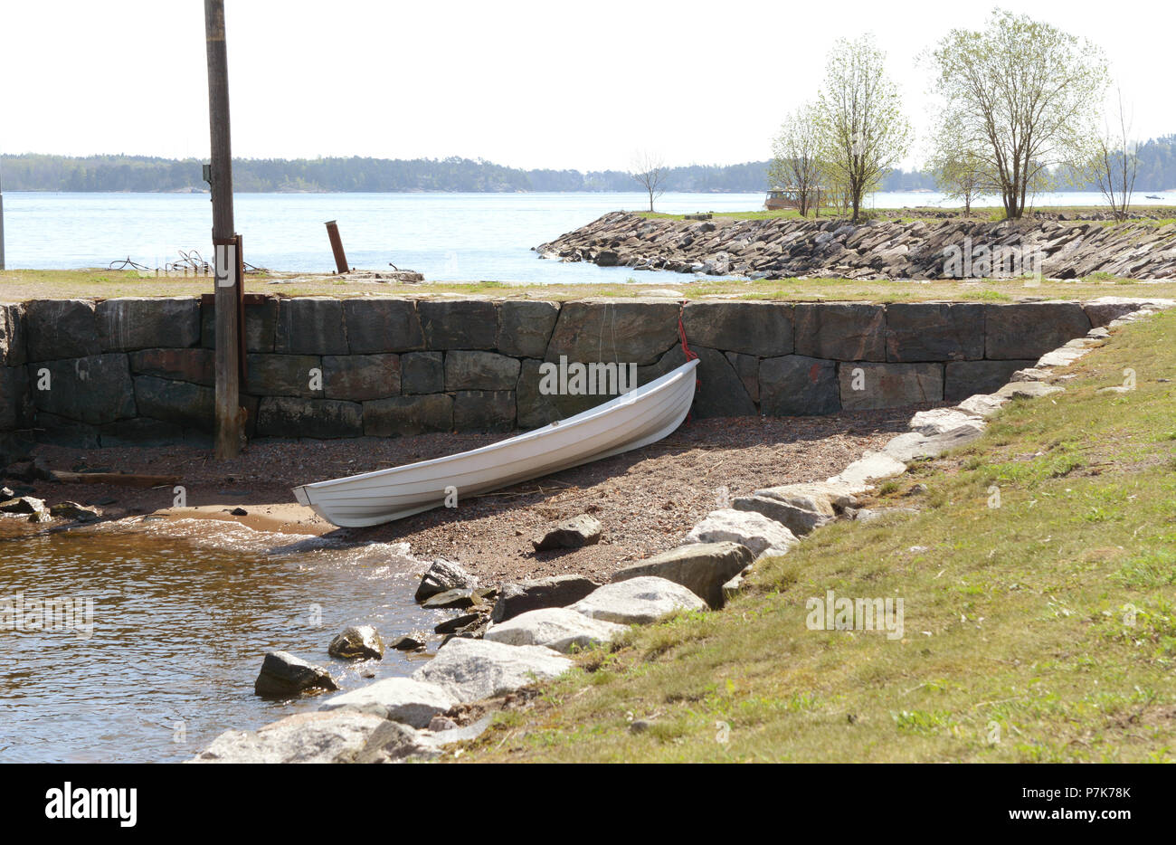 Small white rowboat on a small stony area of shore, against a stone ...