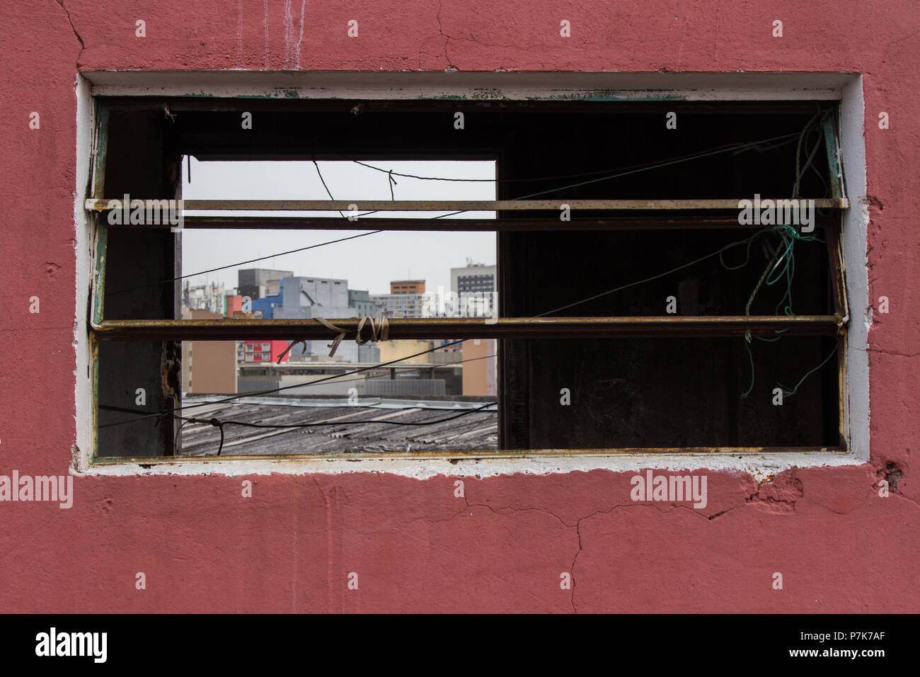 Ruined window with warn blinds with no glass and shabby red walls. City ...