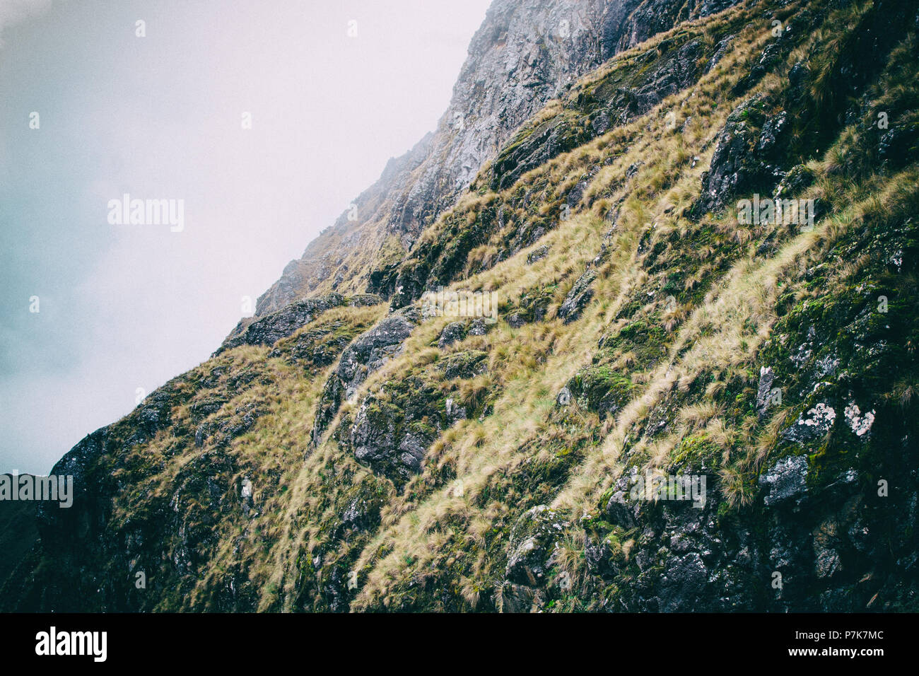 Side of an Andes mountain with rocks and grass and clouds in the ...