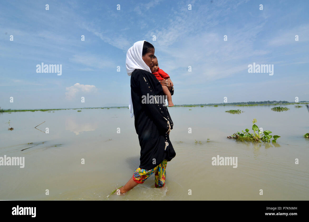 Assam, India. 7th July, 2018. A lady with her baby walks in flooded ...