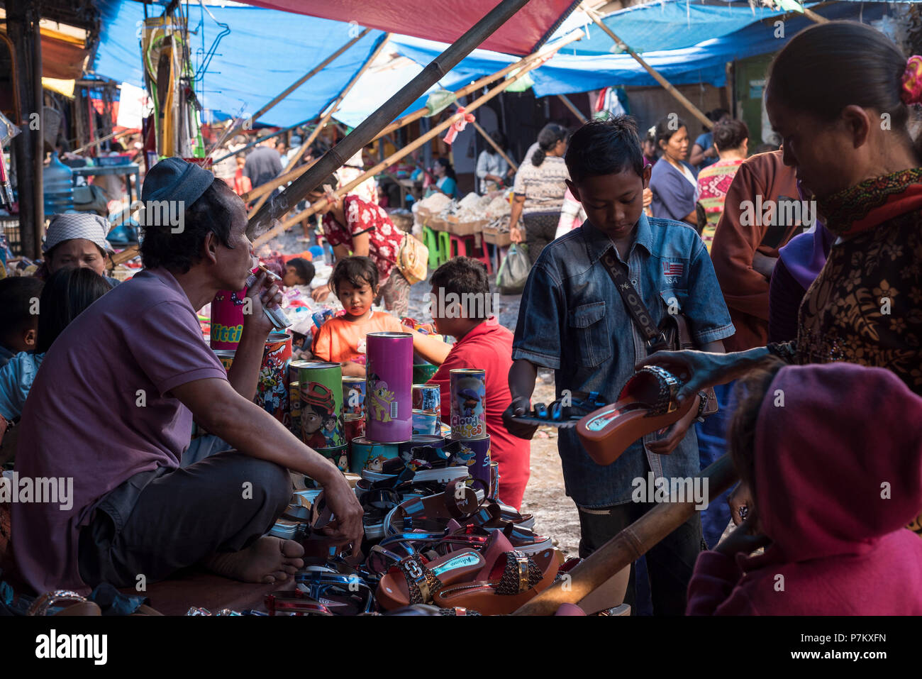 A shoe vendor sitting at his market stall while customers looking at ...