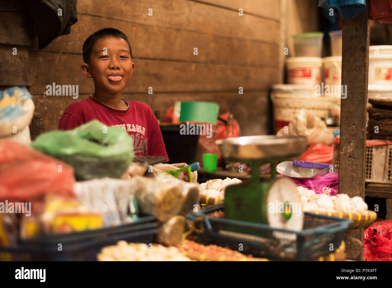 A little boy selling vegetables and spices at a market stall and laughs ...