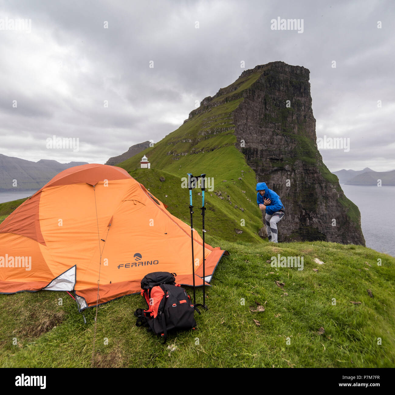 Hiker and tent on cliffs around Kallur Lighthouse, Kalsoy island, Faroe ...