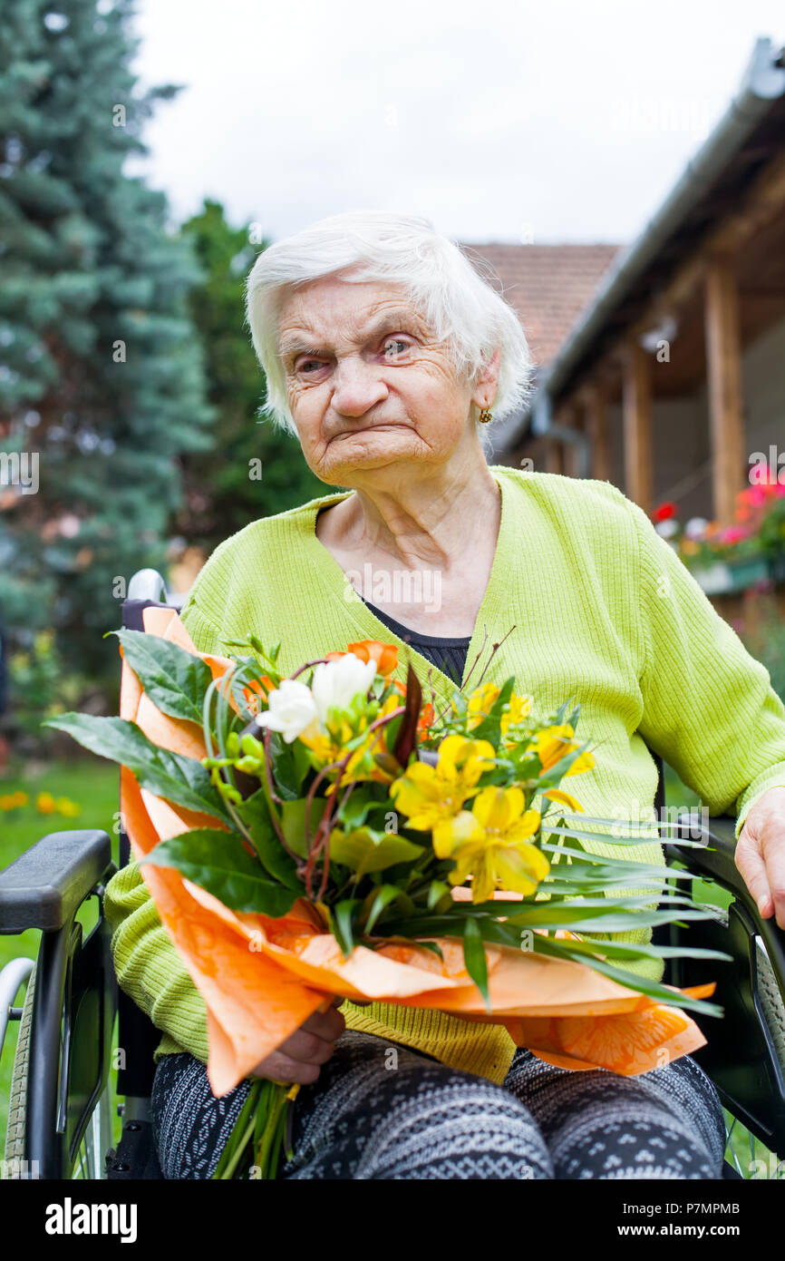 Disabled elderly woman sitting in wheelchair, receiving a flower ...