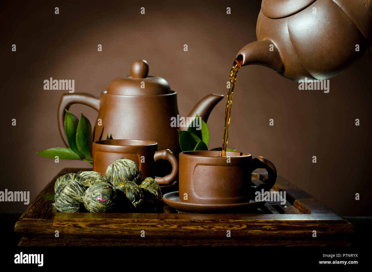 horizontal photo, of the clay teapot tea flow in cup on brown ...