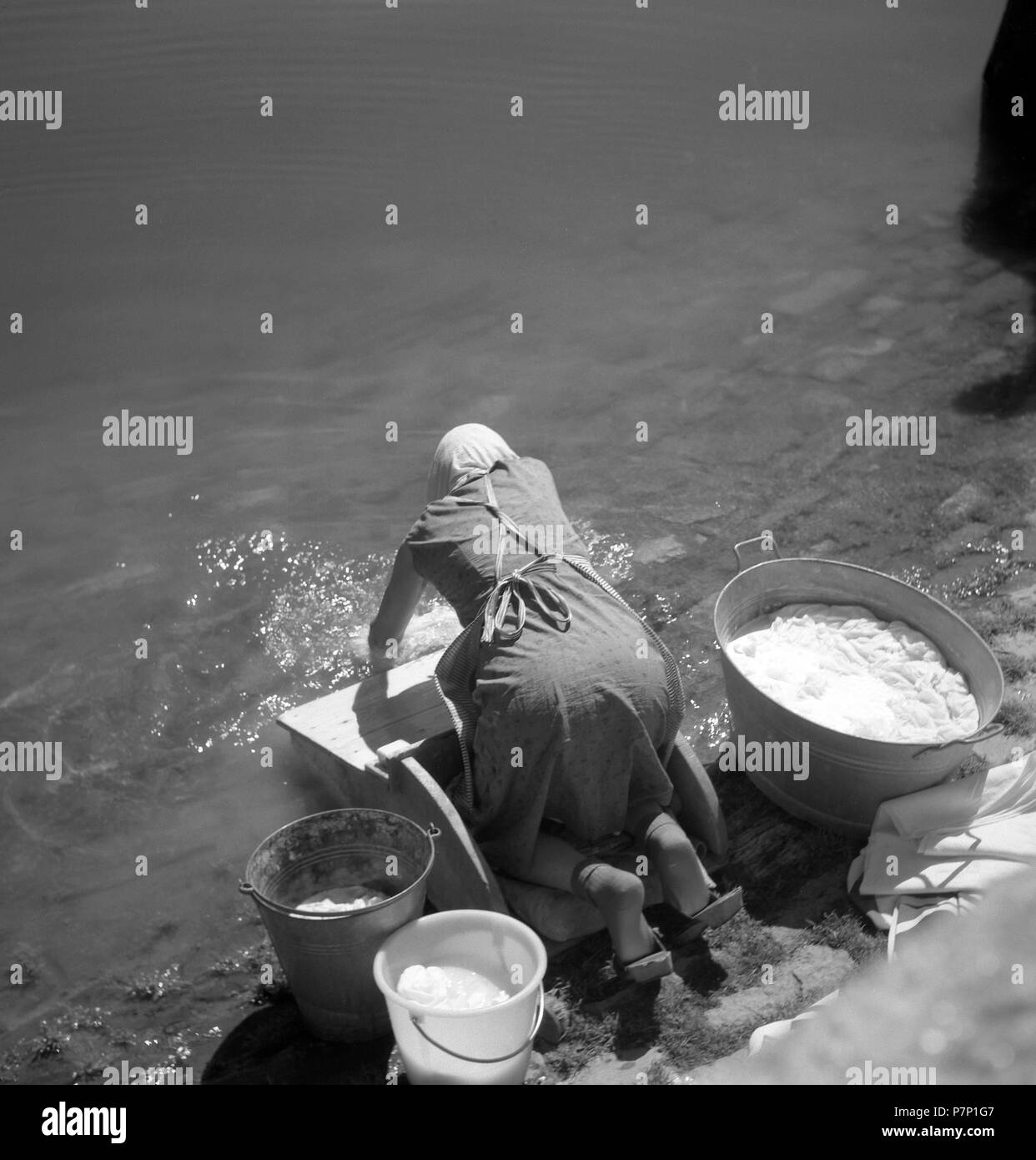 Woman washes her clothes in an old-fashioned way in the river around ...