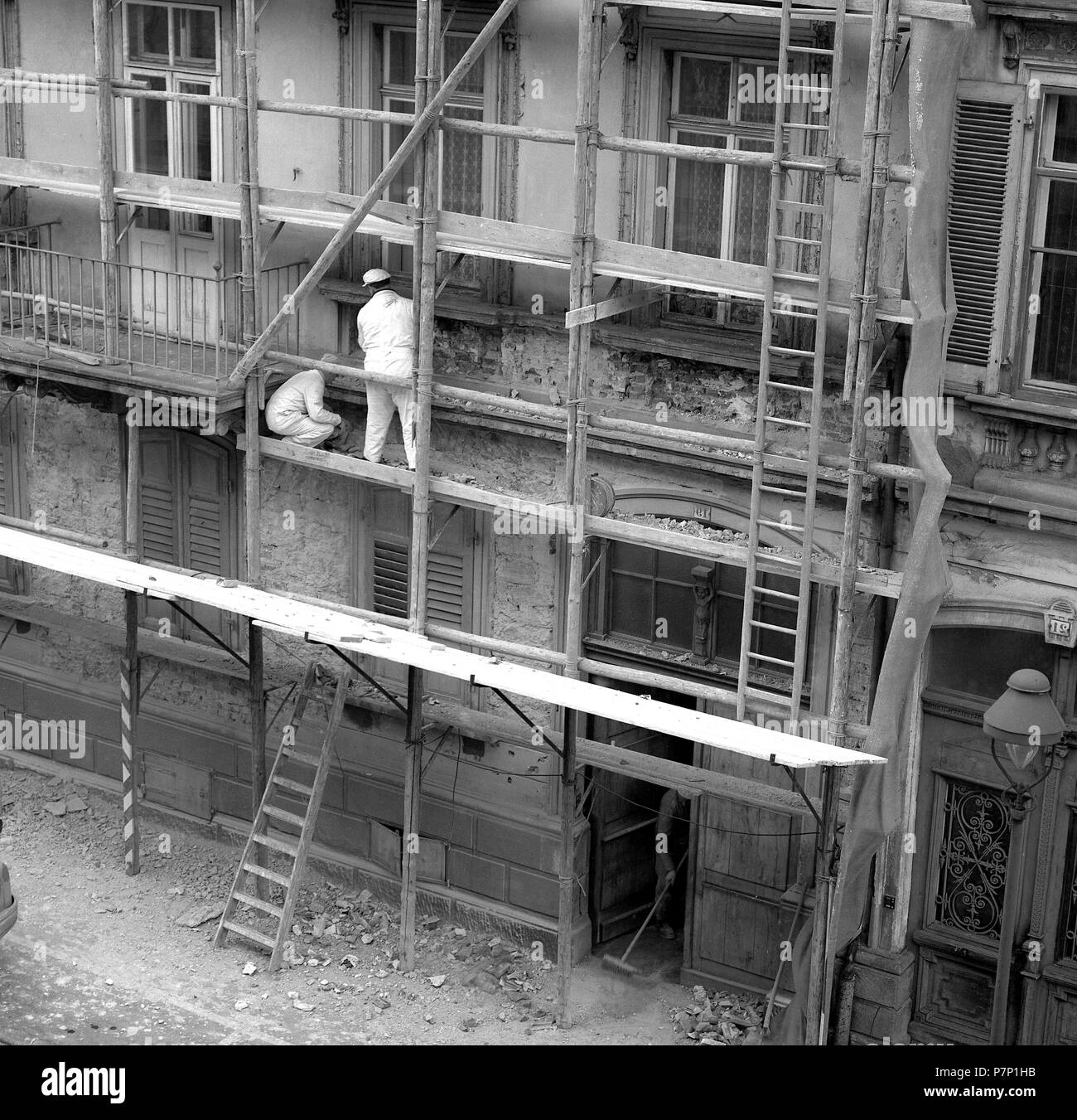 Two construction workers renovate the facade of a house around 1950 ...