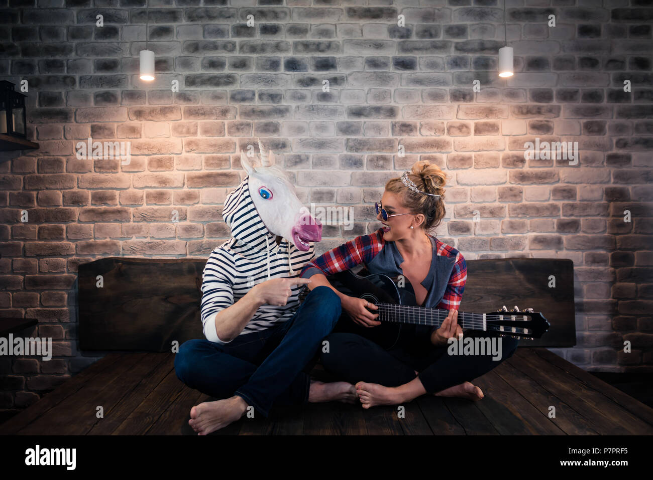 Blonde girl playing music on guitar for freaky man in comical mask ...