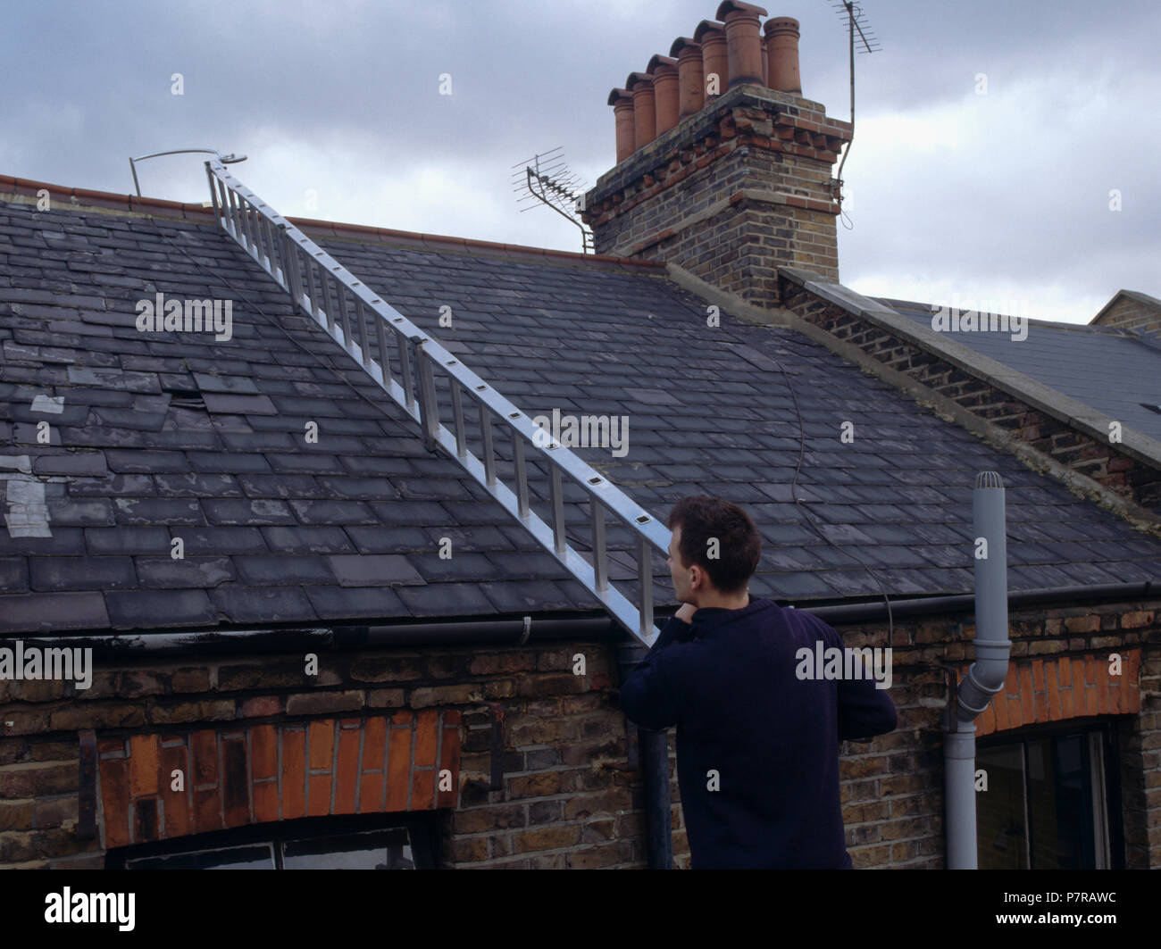 Man positioning ladder on slate roof FOR EDITORIAL USE ONLY Stock Photo ...