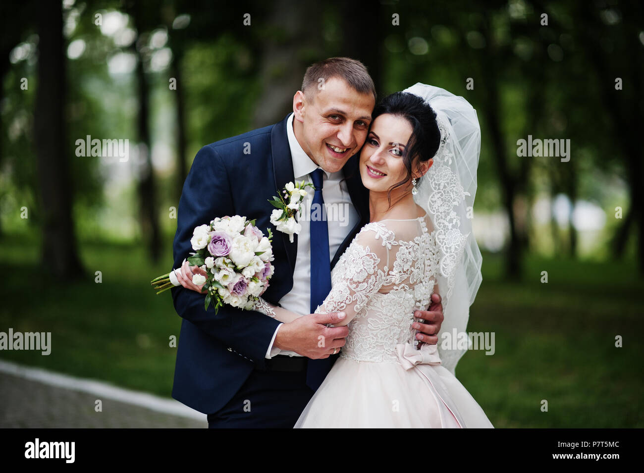 Gorgeous and happy newly married couple standing in green park on their ...