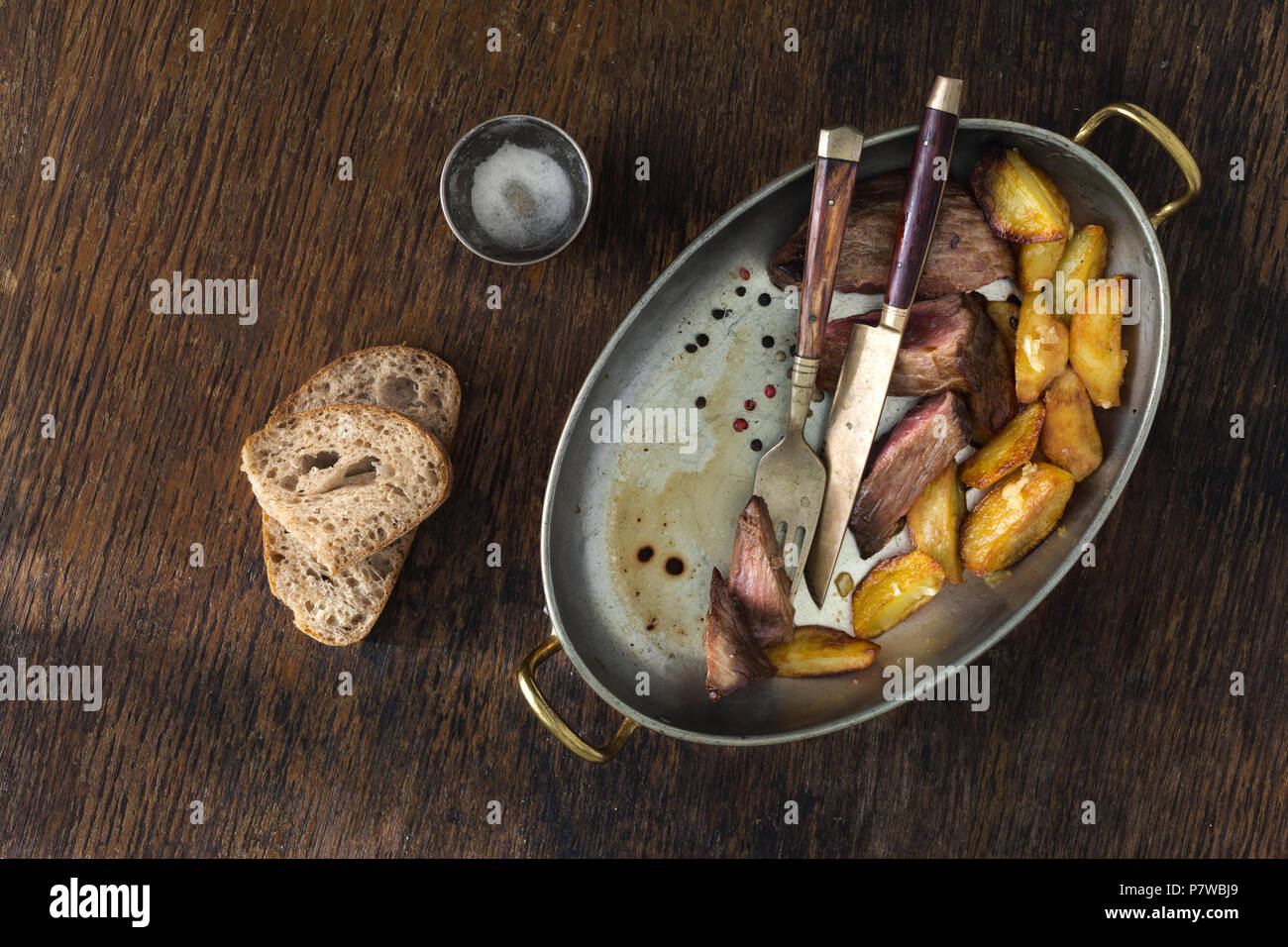 Top view beef steak with fried potatoes in frying pan on dark ...