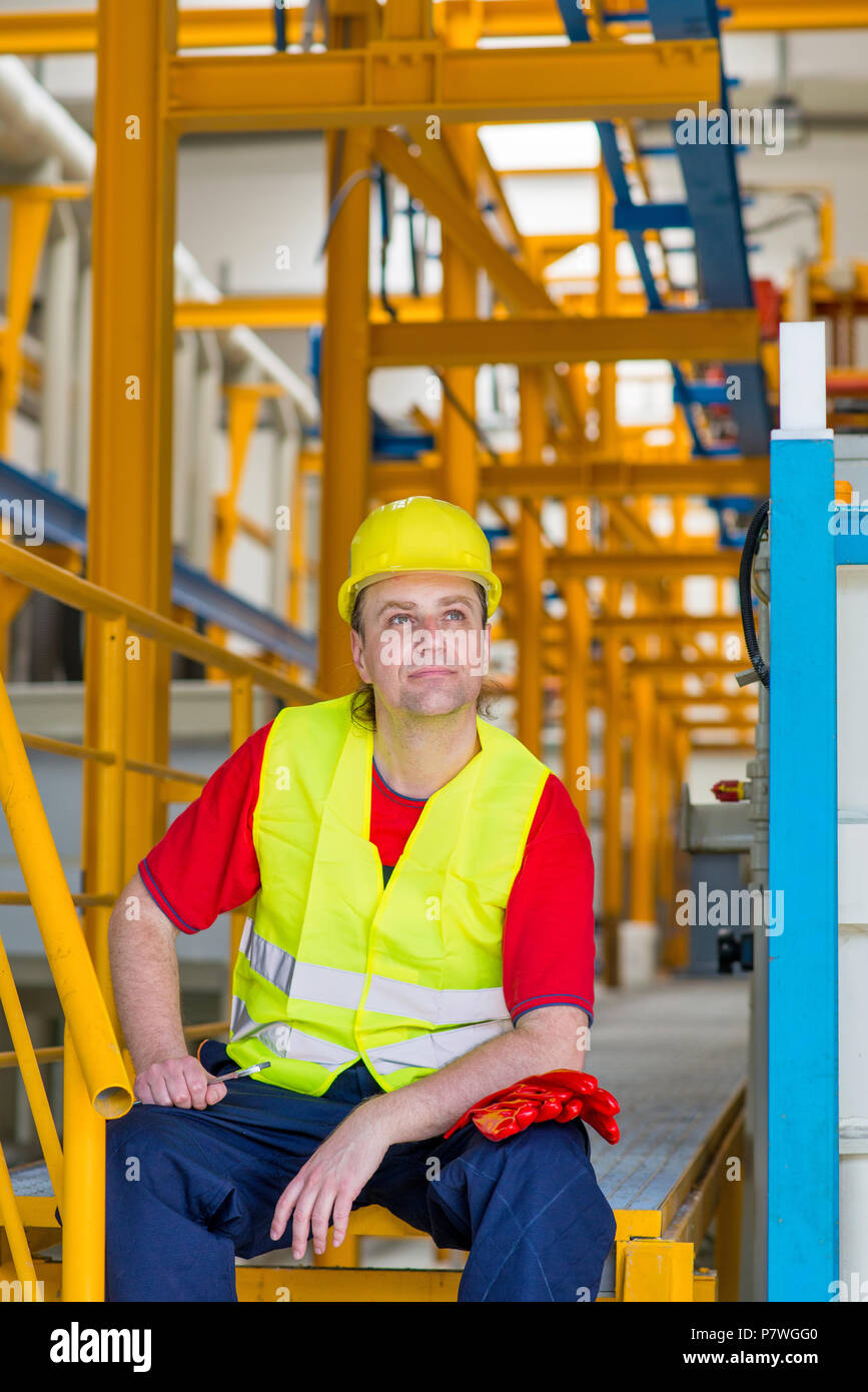 Worker in yellow reflective suit with yellow helmet sitting in a ...