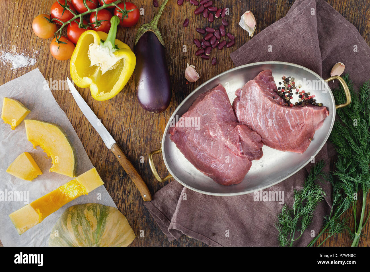 Fresh beef tenderloin in a frying pan on a wooden table with vegetables ...