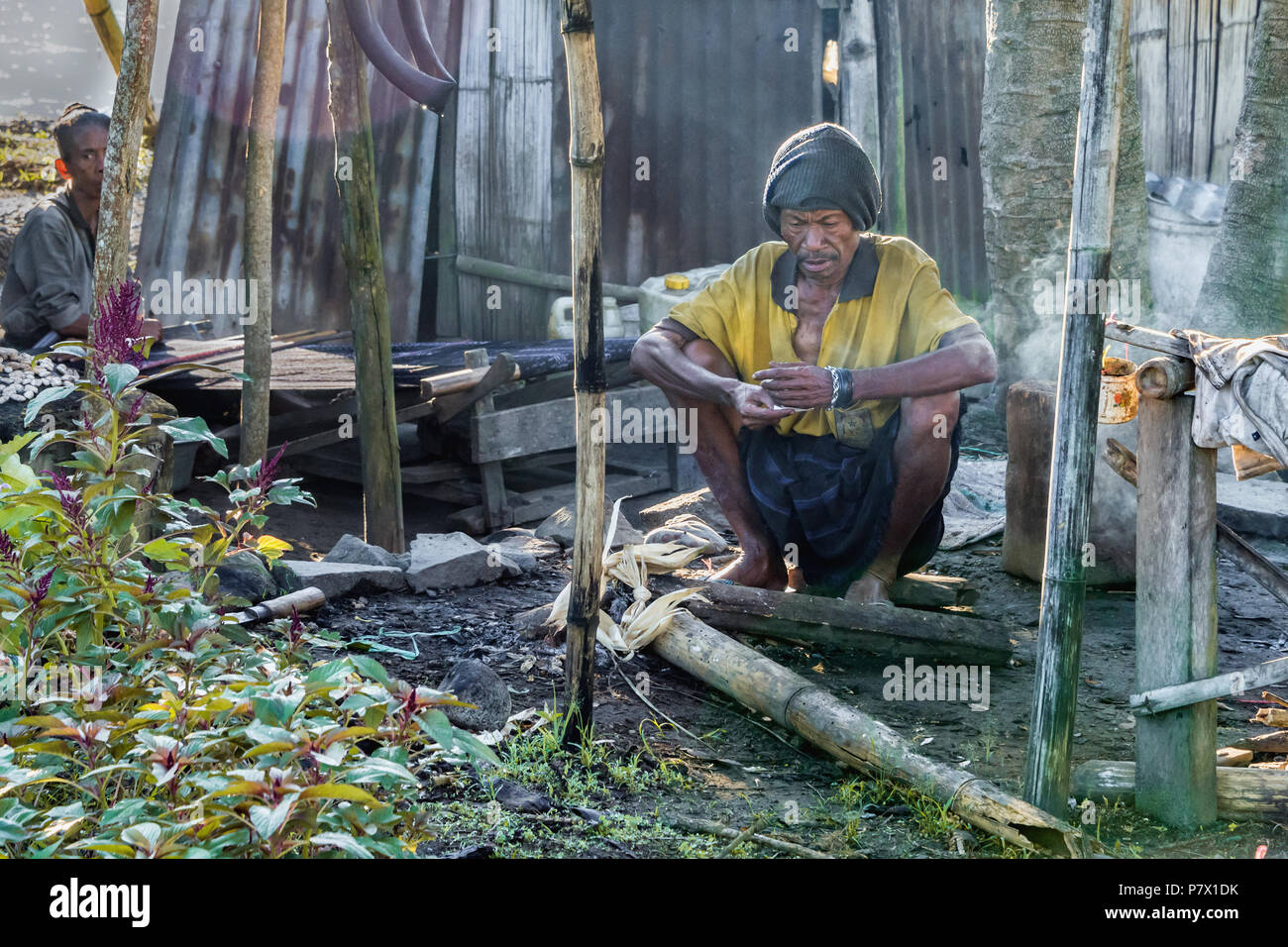 Man rolling a morning cigarette next to a cooking fire, Moni, East Nusa ...