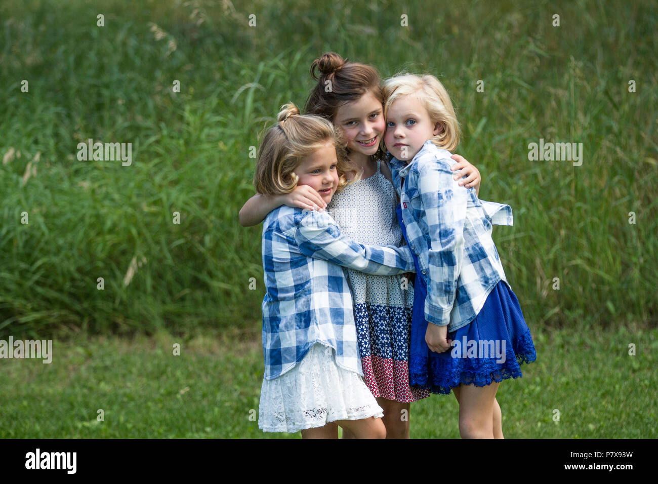 3 friends posing, as group, outdoors. Arms around shoulder and looking ...