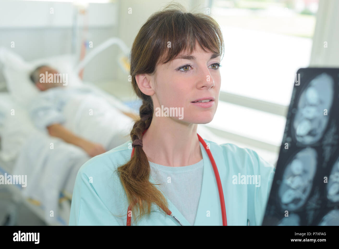 Medic looking at scan results, patient in hospital bed in background ...