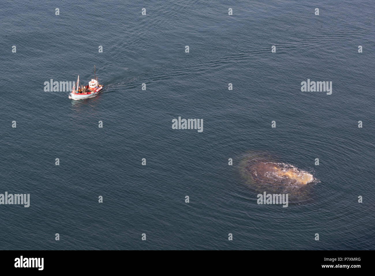 small inshore fishing boat next to a rock on the coast in the open sea ...