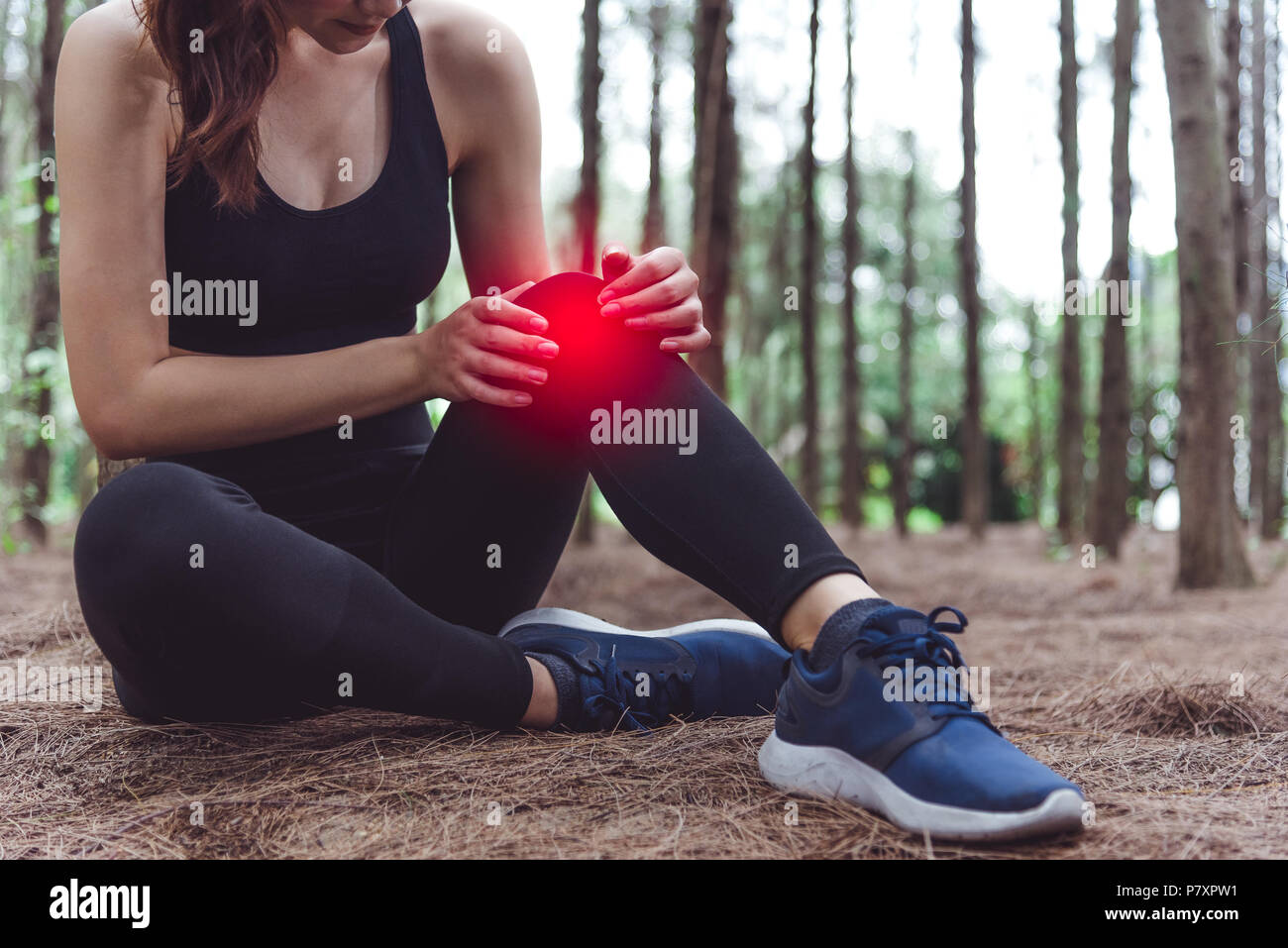 Sport woman injury at knee during jogging in forest. Pine woods ...
