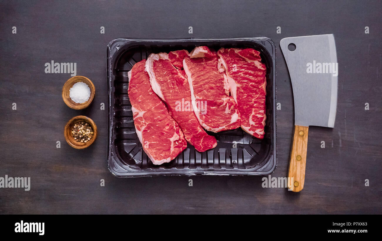 Raw New York strip steaks in black plastic meat packaging container ...