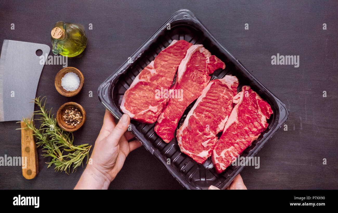 Raw New York strip steaks in black plastic meat packaging container ...