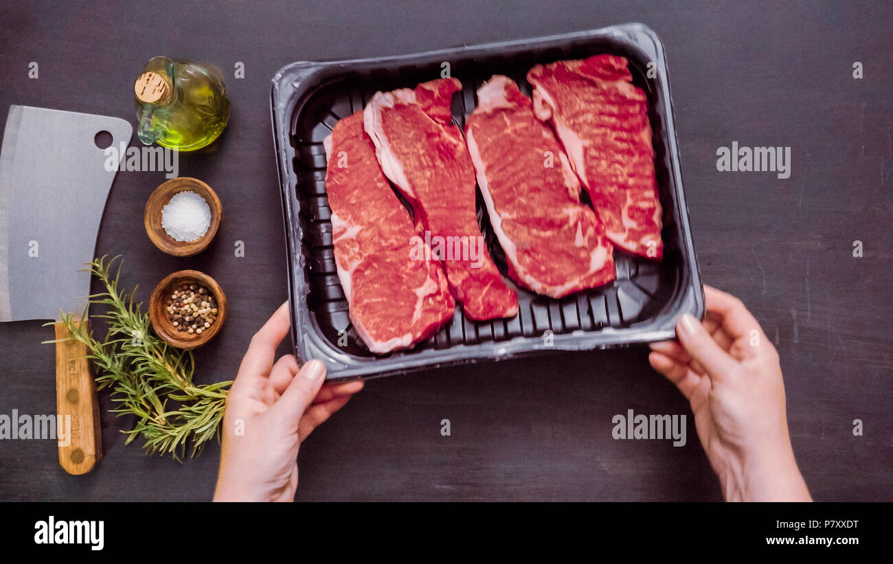 Raw New York strip steaks in black plastic meat packaging container ...