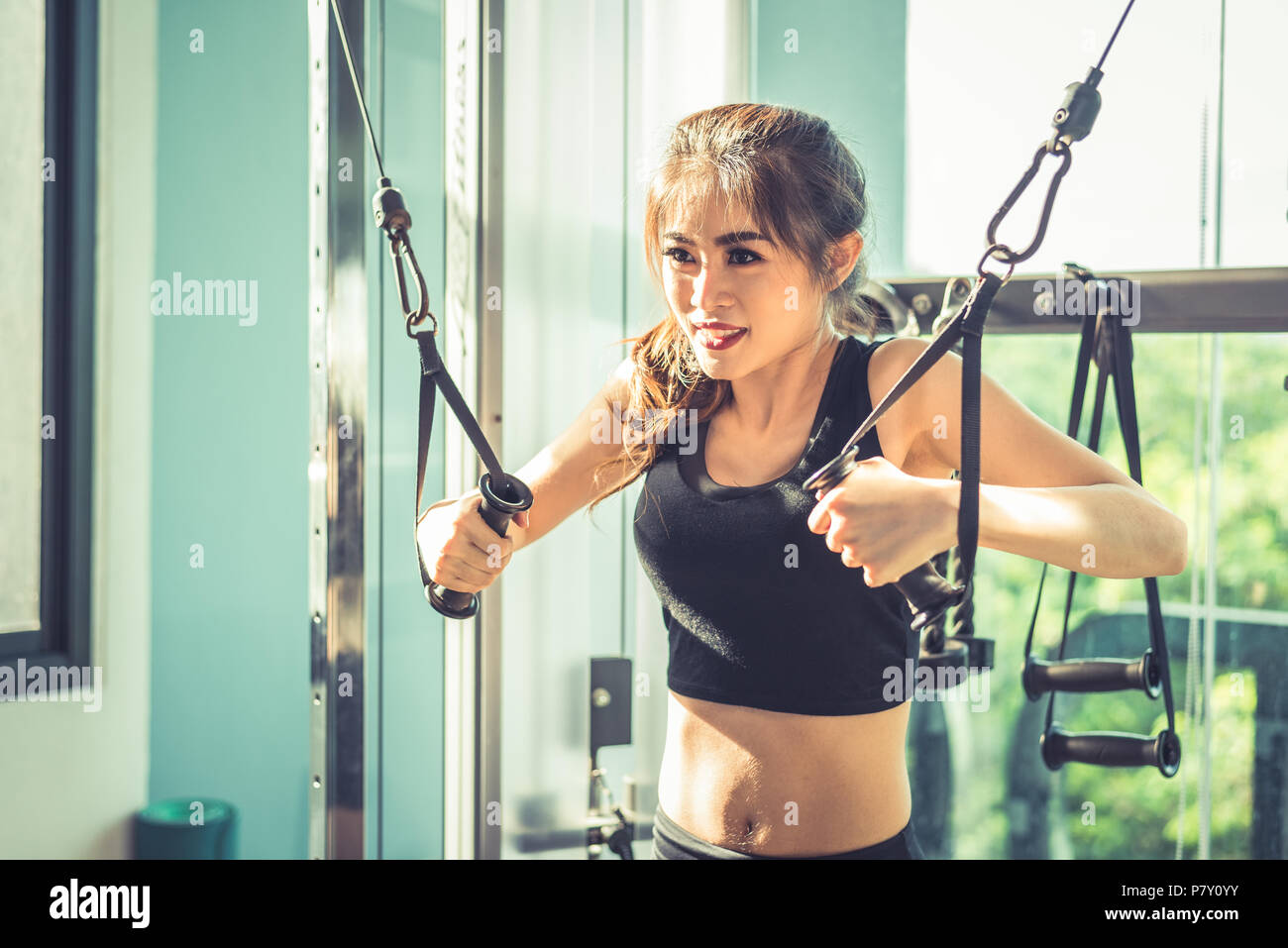 Asian young woman doing elastic rope exercises at cross fitness gym ...