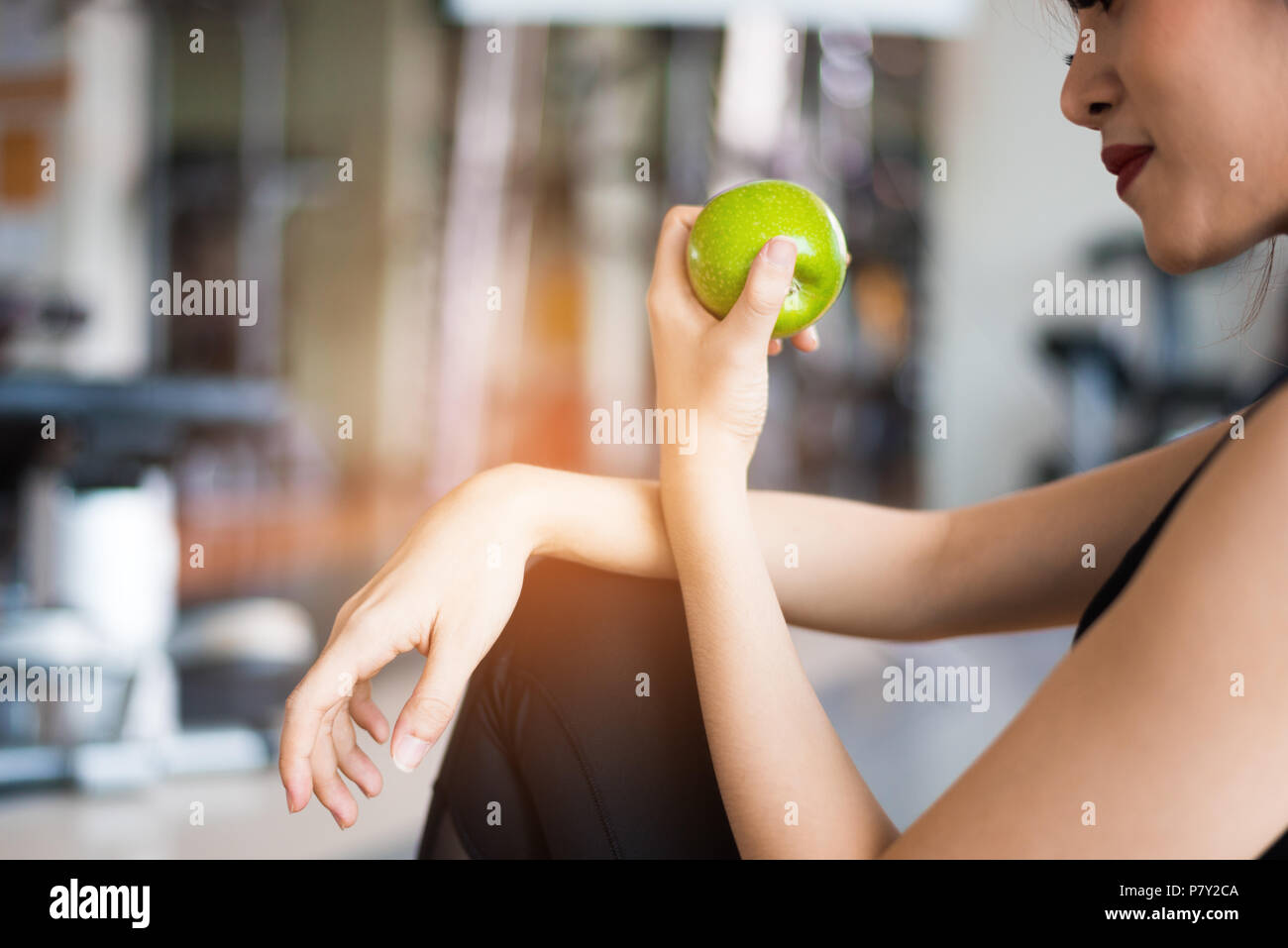 Sports woman sitting and eating green apple in fitness training gym ...