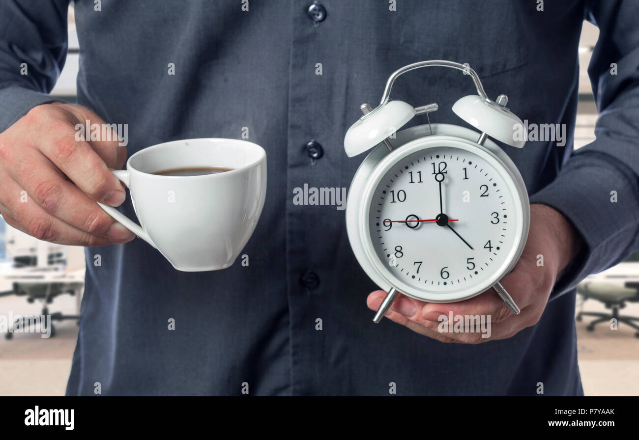 The office worker holds a cup of aromatic coffee and an alarm clock ...