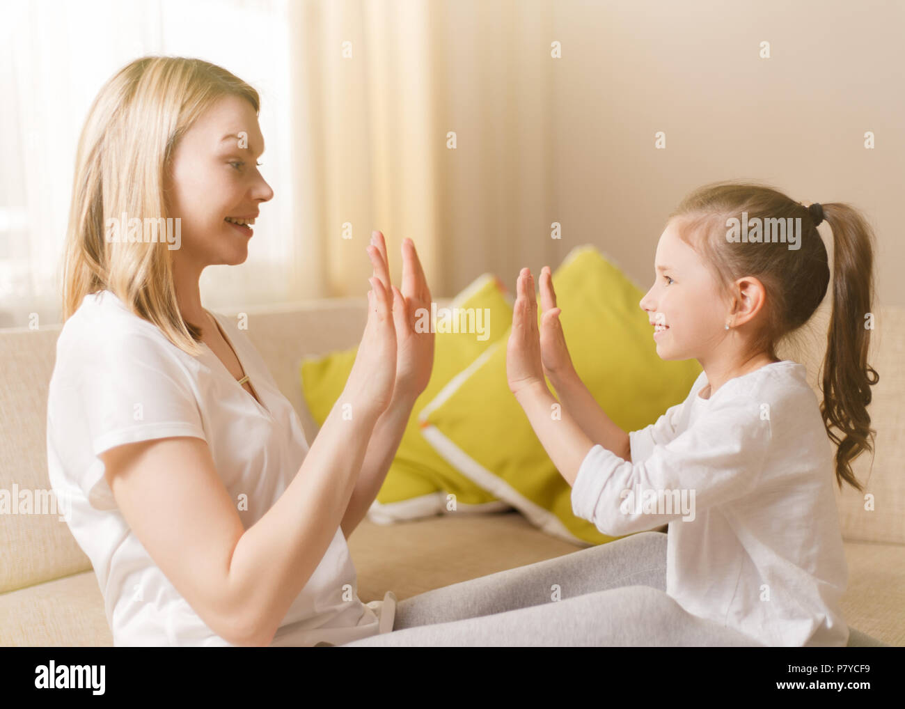 Cute little girl and her beautiful mother are playing games at home, clapping hands together ...