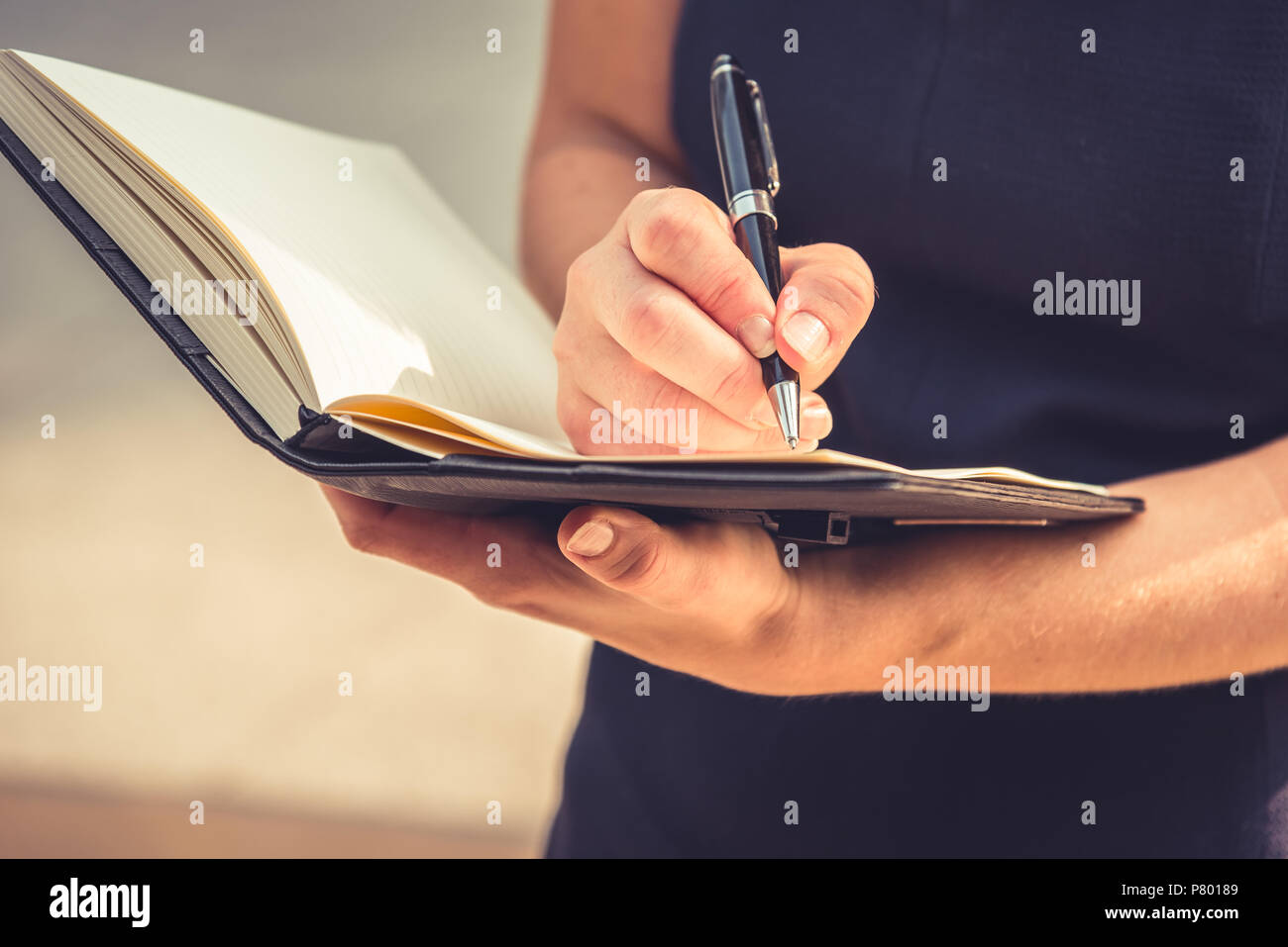Closeup of young woman writing down letters in notepad for making note ...