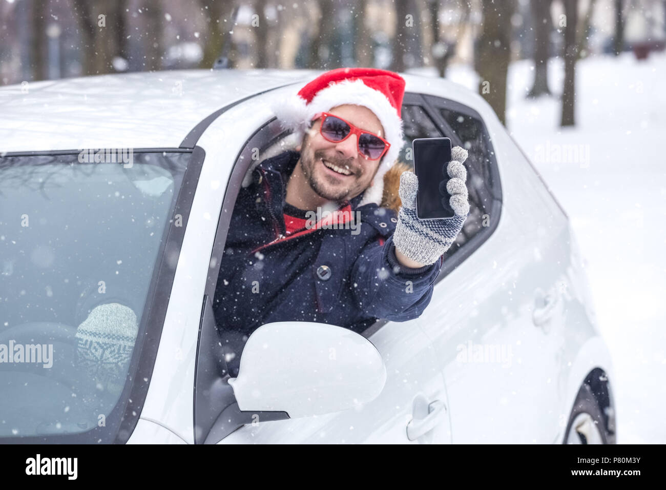 Driver with santa hat and sunglasses showing blank screen smartphone ...