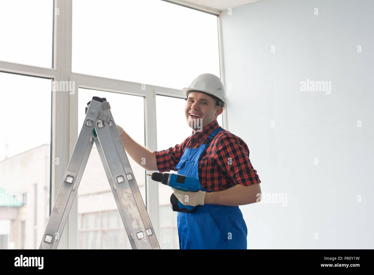 Happy male builder standing on ladder with drill infront of window ...